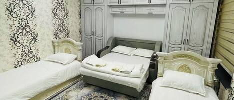 Quarto com uma cama grande, duas camas menores, um tapete estampado e um lustre.