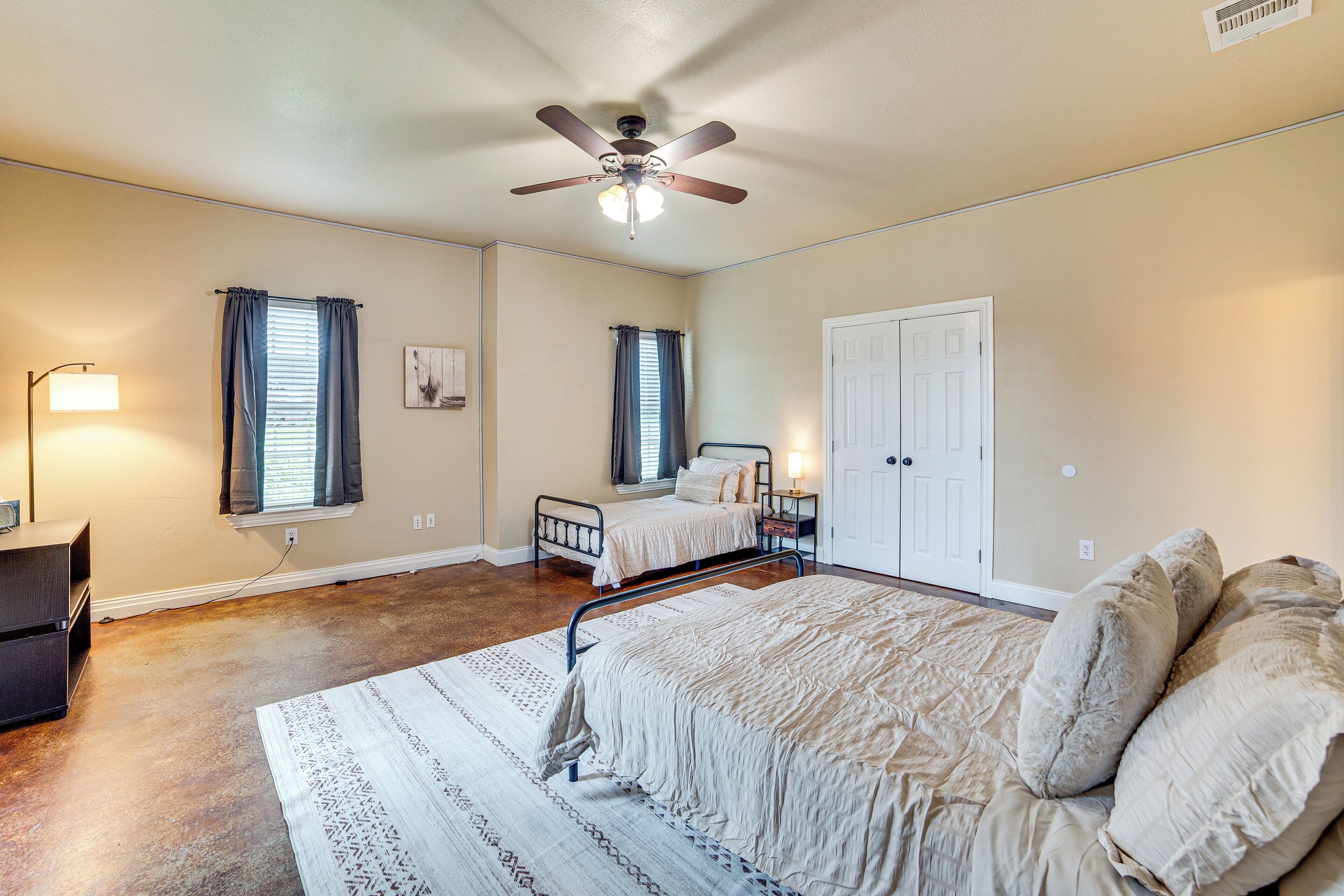 Quarto com cama, ventoinha no teto, janela com cortinas, mesa de cabeceira e porta.