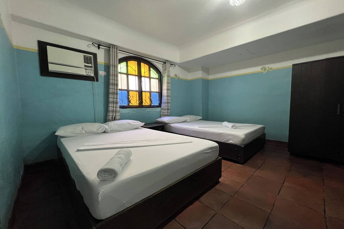 Quarto com duas camas, uma janela com cortinas, um espelho e um guarda-roupa.