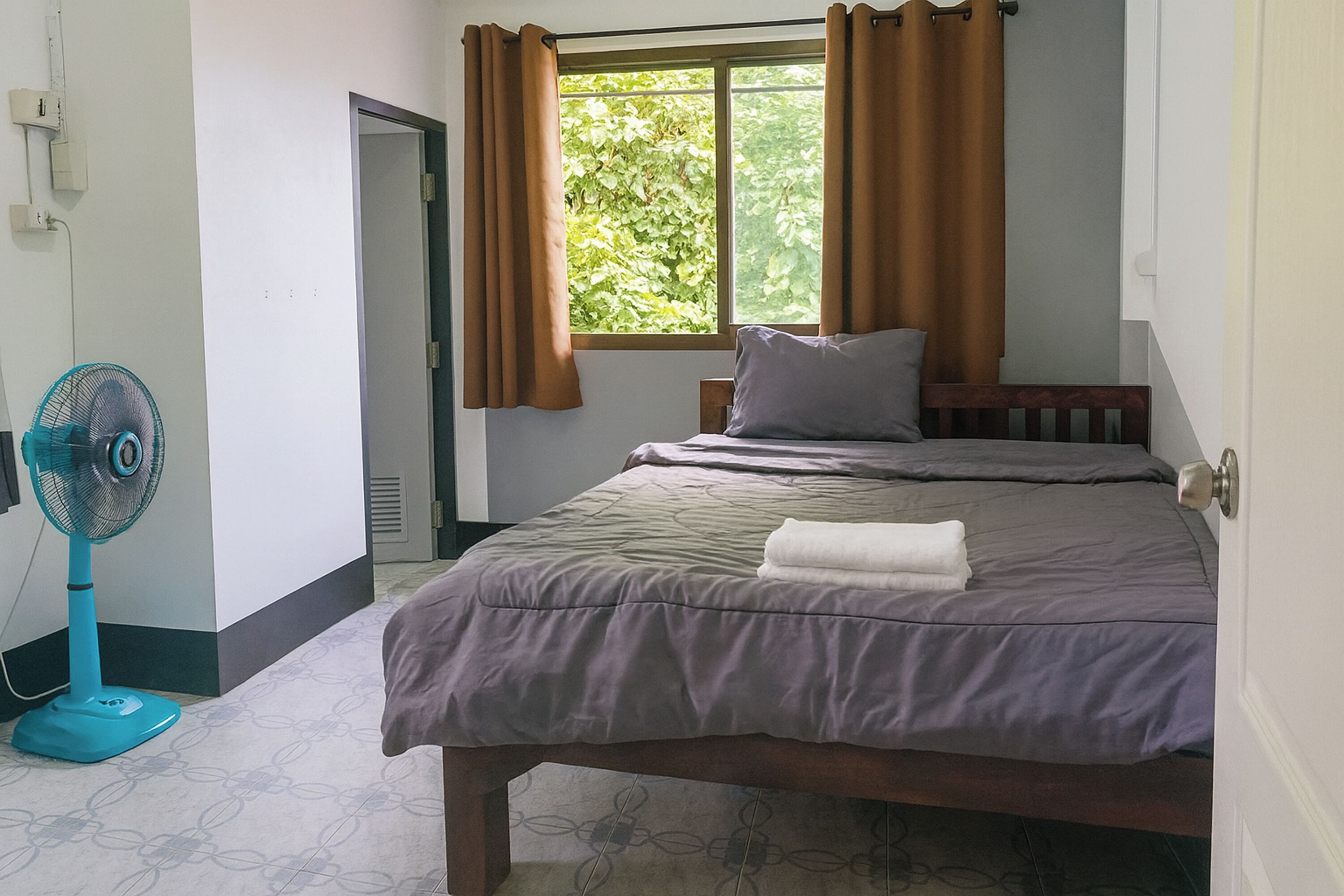 Quarto com cama, janela com cortinas, ventilador e porta.