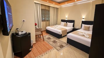 Quarto de hotel com duas camas, uma escrivaninha com computador e máquina de café, uma televisão e uma janela grande com cortinas.