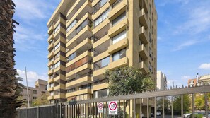 Edifício residencial com vários andares, varandas, cerca de metal e placa de proibição de estacionamento.