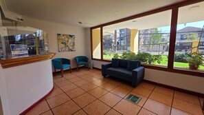 Quarto com uma janela grande, um sofá, duas cadeiras e uma pequena mesa com um aviso.