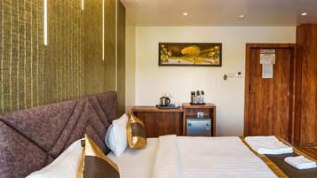 Quarto de hotel com cama, mesa de cabeceira, cafeteira e geladeira.