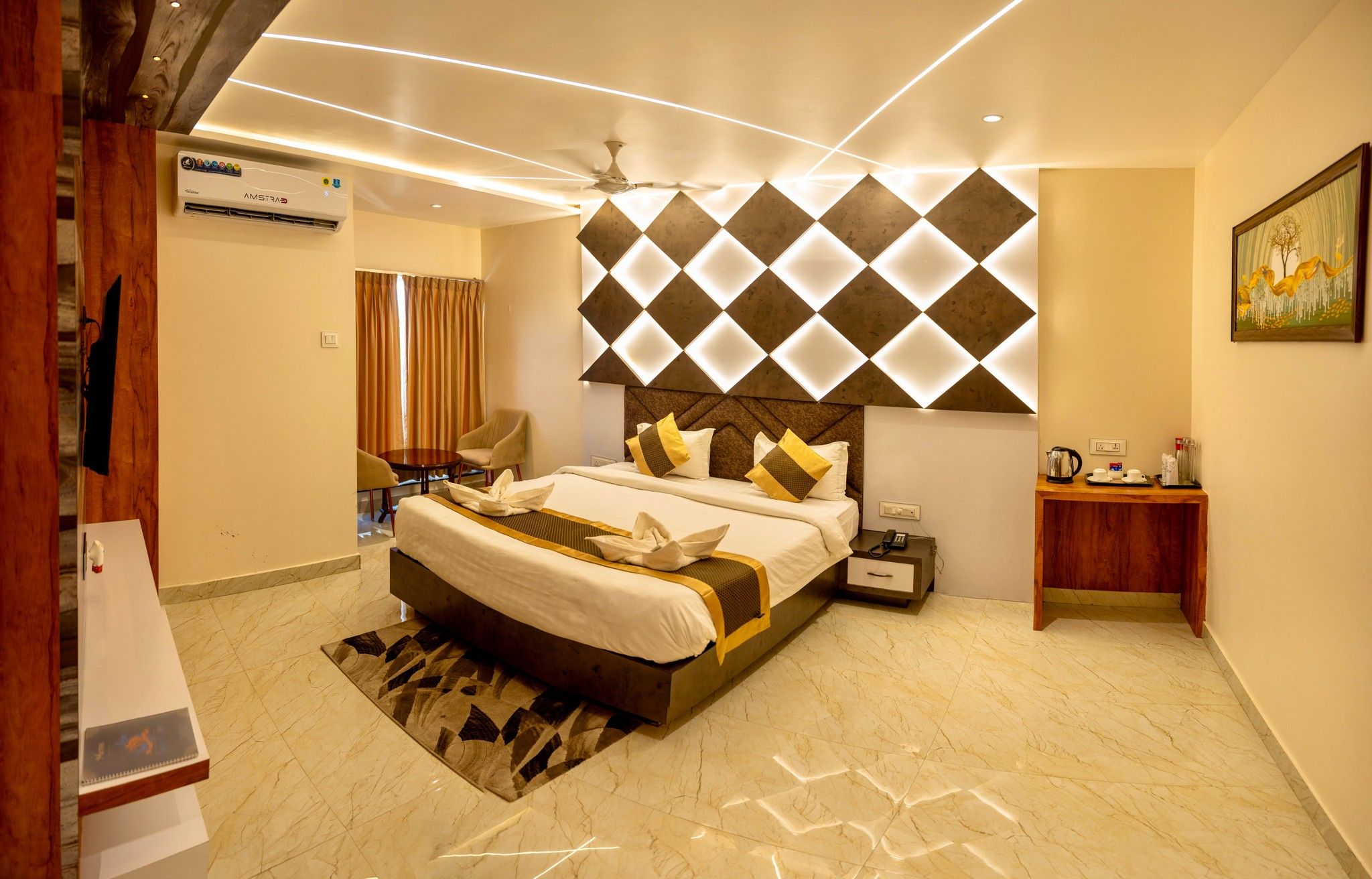 Quarto de hotel moderno com uma cama grande, escrivaninha, cadeira, mesa de cabeceira e ventoinha no teto.