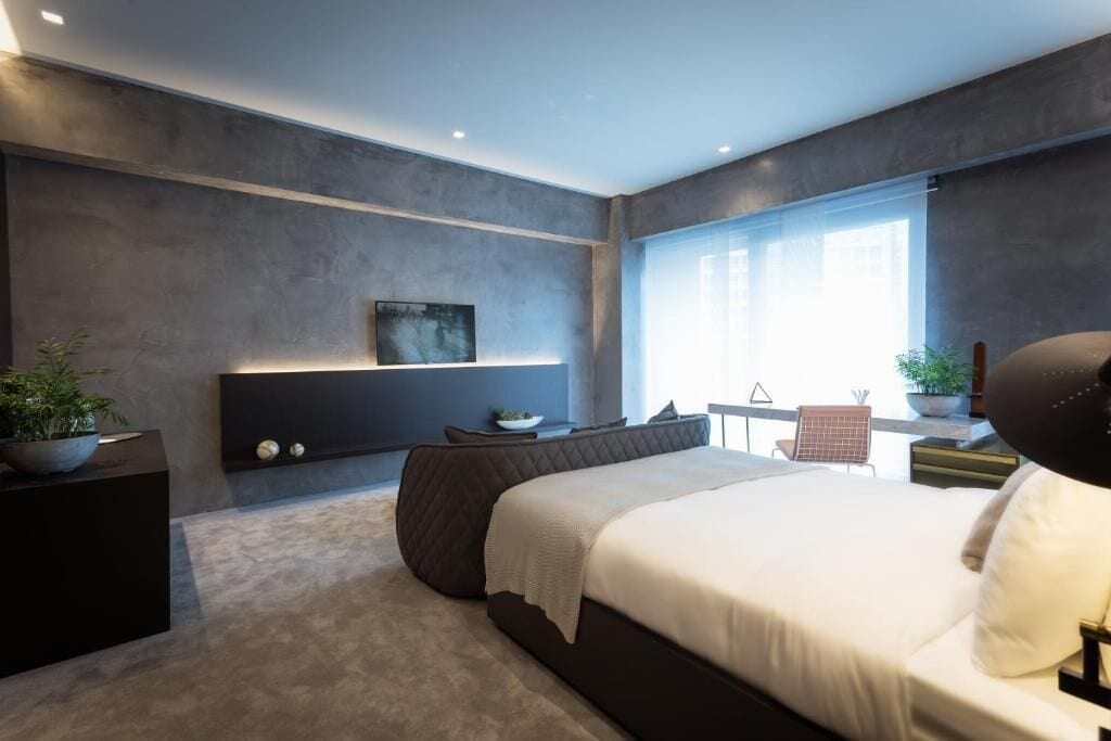 Quarto moderno com uma cama grande, mesa de cabeceira, televisão na parede e janela com vista.