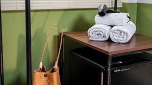 Um quarto com uma mesa de madeira, um refrigerador preto, uma sacola de tecido e uma pilha de toalhas.