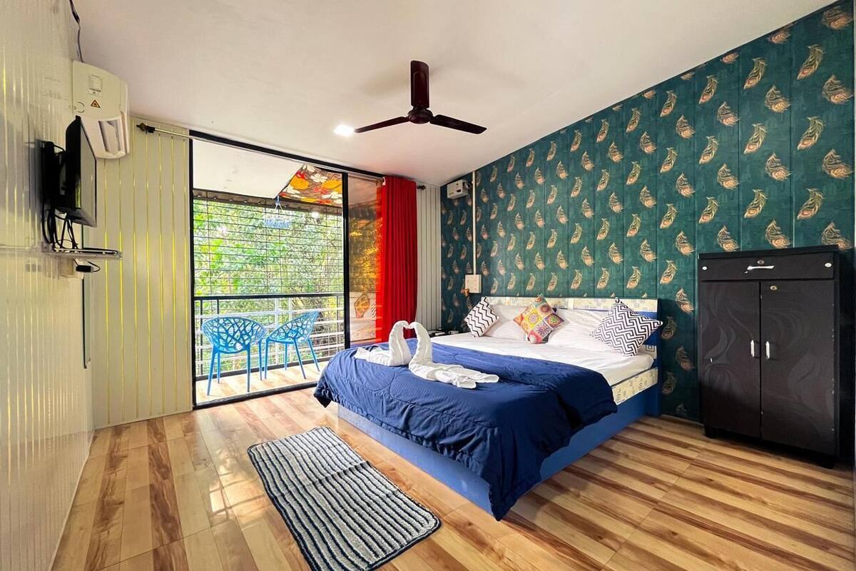 Quarto com cama, guarda-roupa, ventoinha no teto, janela com vista e varanda com cadeiras.