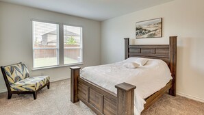 Quarto com uma cama grande, uma cadeira e duas janelas.