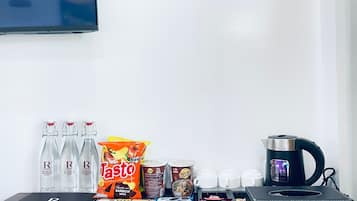 Quarto de hotel com minibar que inclui garrafas de água, um saco de chips Tostitos, uma lata de café e uma chaleira.