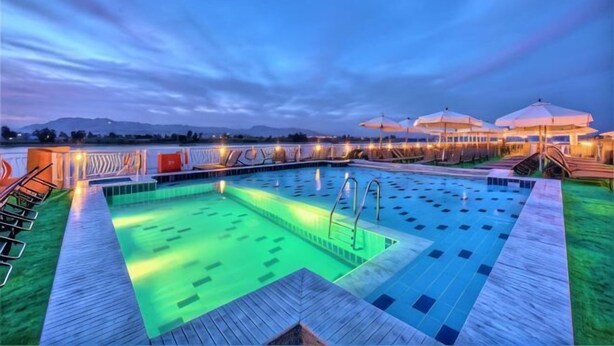 Uma piscina com deck de madeira, escada e guarda-sóis.