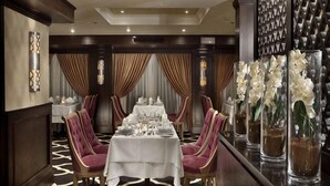 Uma sala de jantar formal com uma mesa comprida posta para refeição, cercada por cadeiras estofadas.