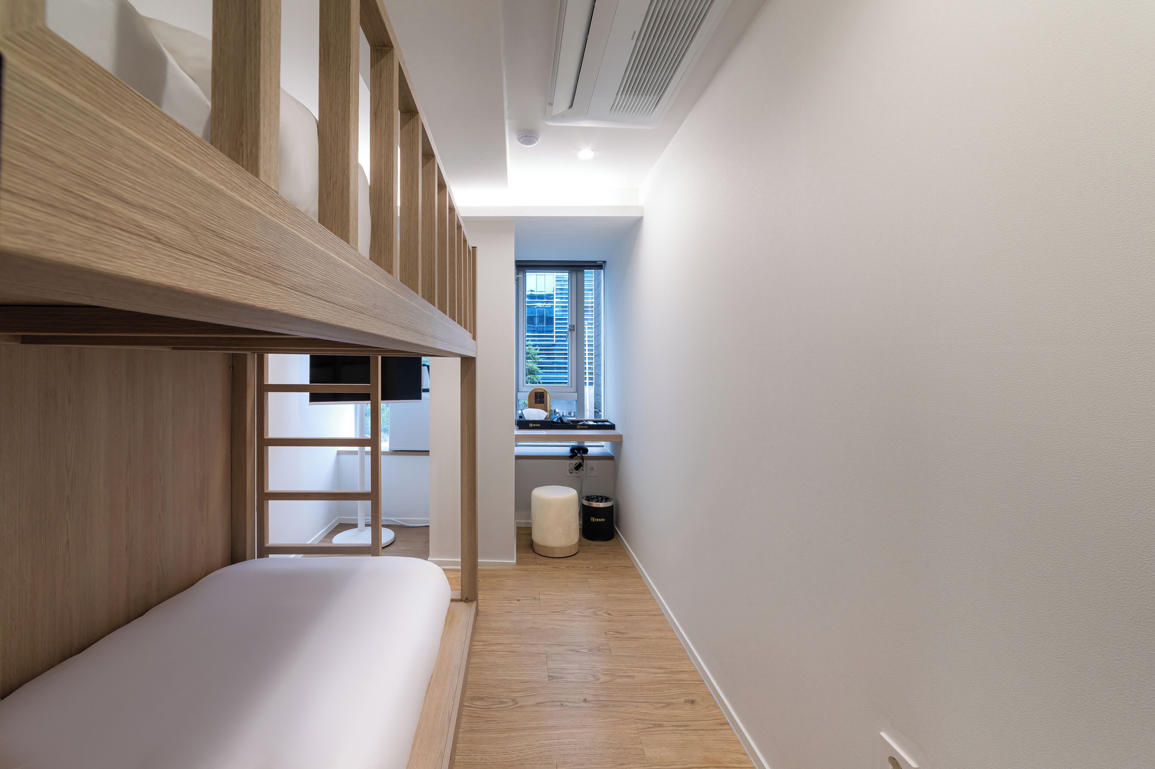 Quarto pequeno com beliche, uma janela e um espaço com cozinha compacta.