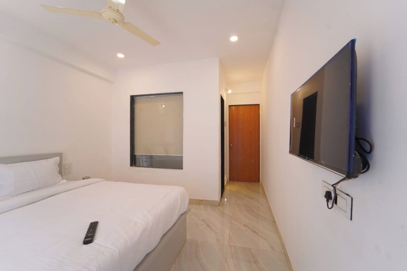 Quarto de hotel com cama, televisão fixada na parede, ventilador de teto e janela.
