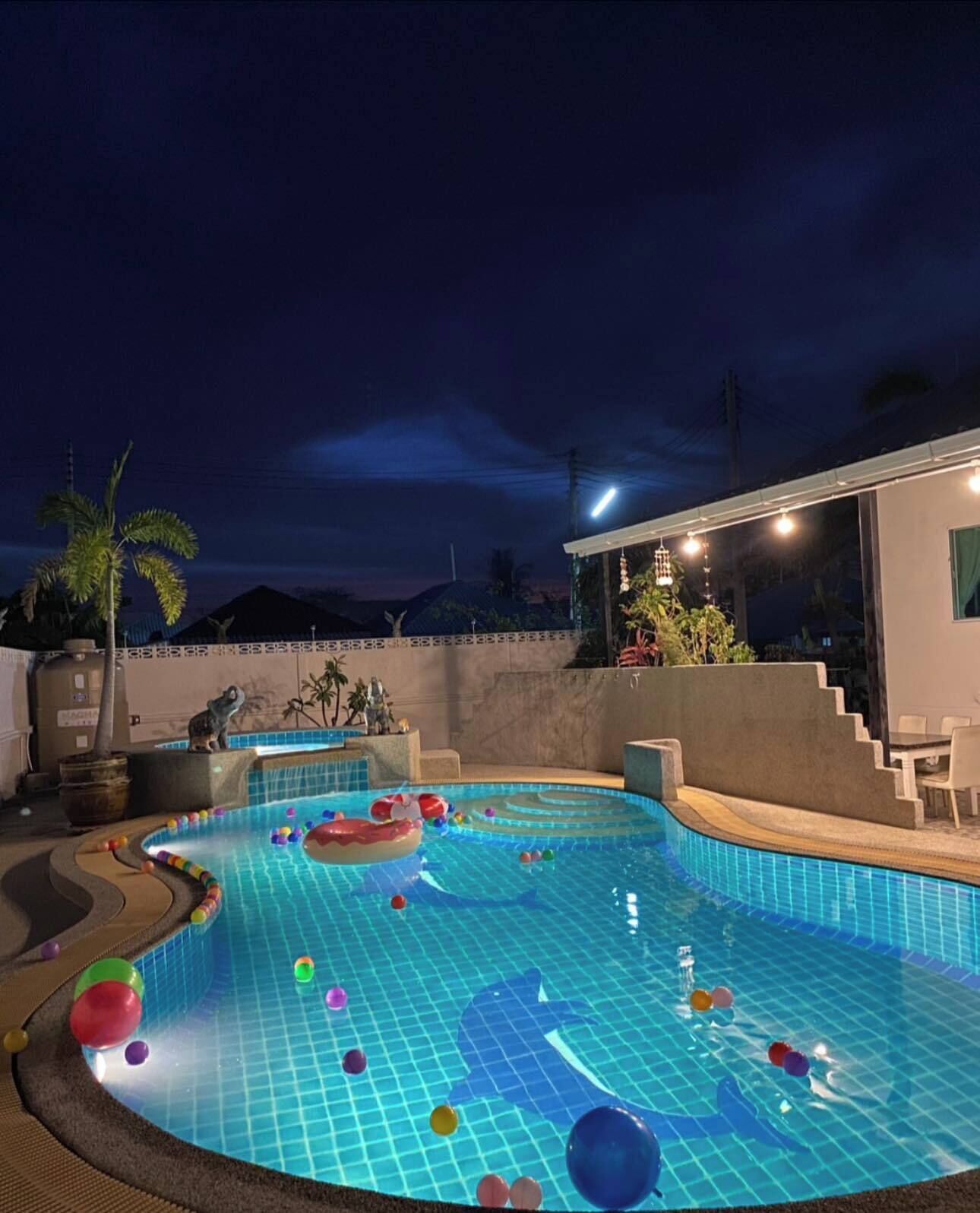 Piscina com design de golfinho no chão, rodeada por um deck com escadas que levam a um espaço coberto com assentos.