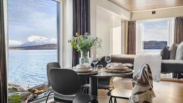 Quarto com mesa de jantar posta para dois, sofá e vista para um lago e montanhas.