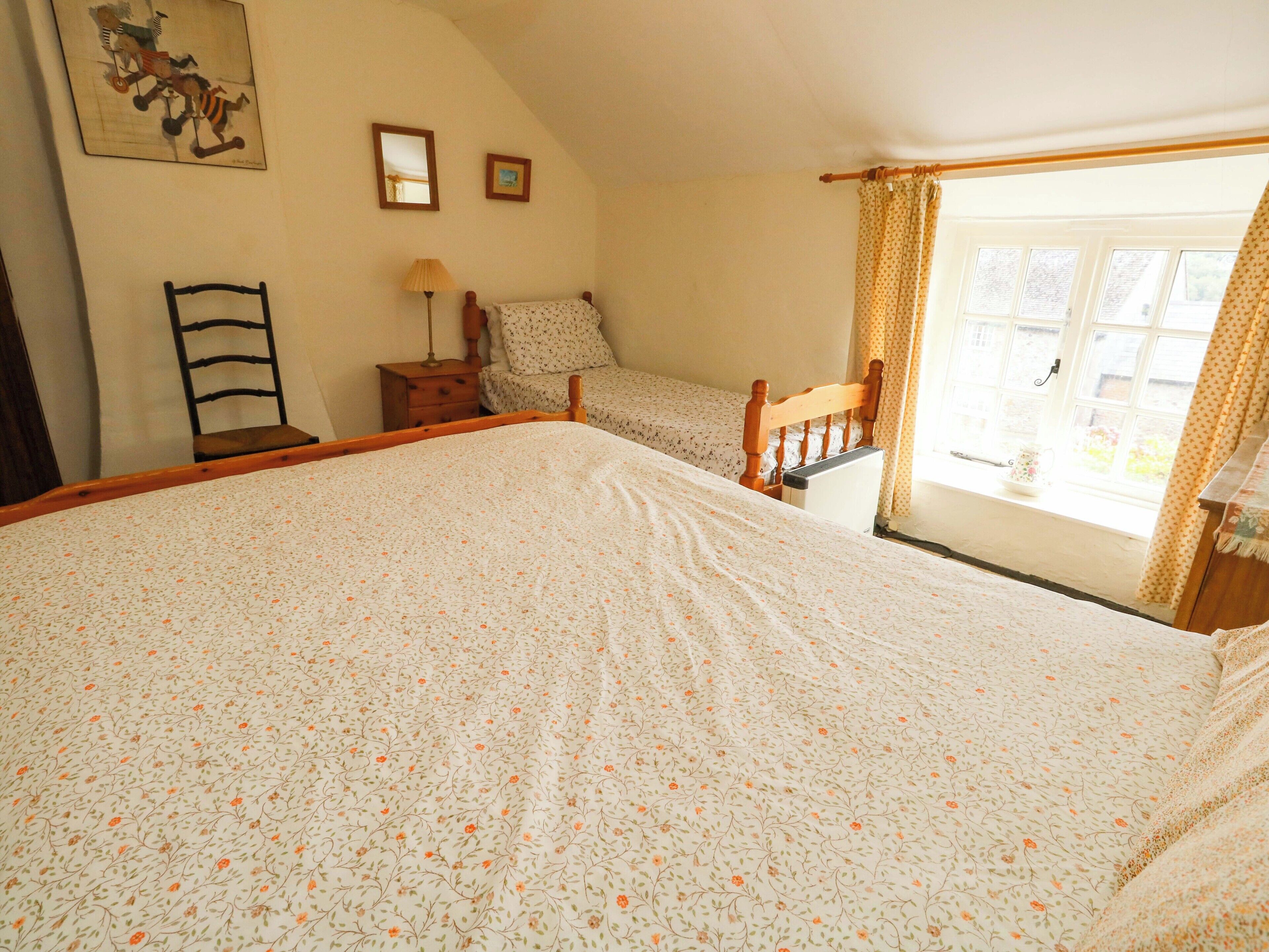 Quarto com cama grande, cadeira de madeira, mesa de cabeceira, luminária e janela com cortinas.