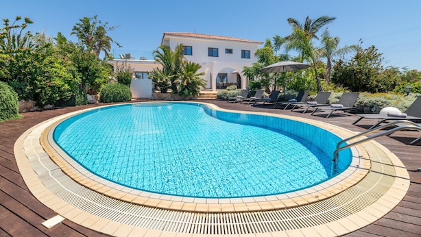 Piscina com deck de madeira, espreguiçadeiras e palmeiras.