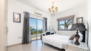 Um quarto com cama, mesa de cabeceira, abajur, janela com vista e lustre.