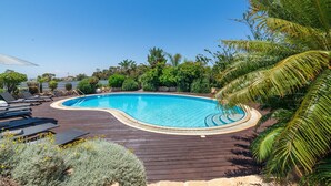 Uma piscina sinuosa com espreguiçadeiras e paisagismo tropical.