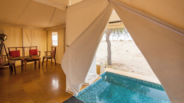 Quarto tipo tenda com piscina, móveis de madeira e vista para o deserto.