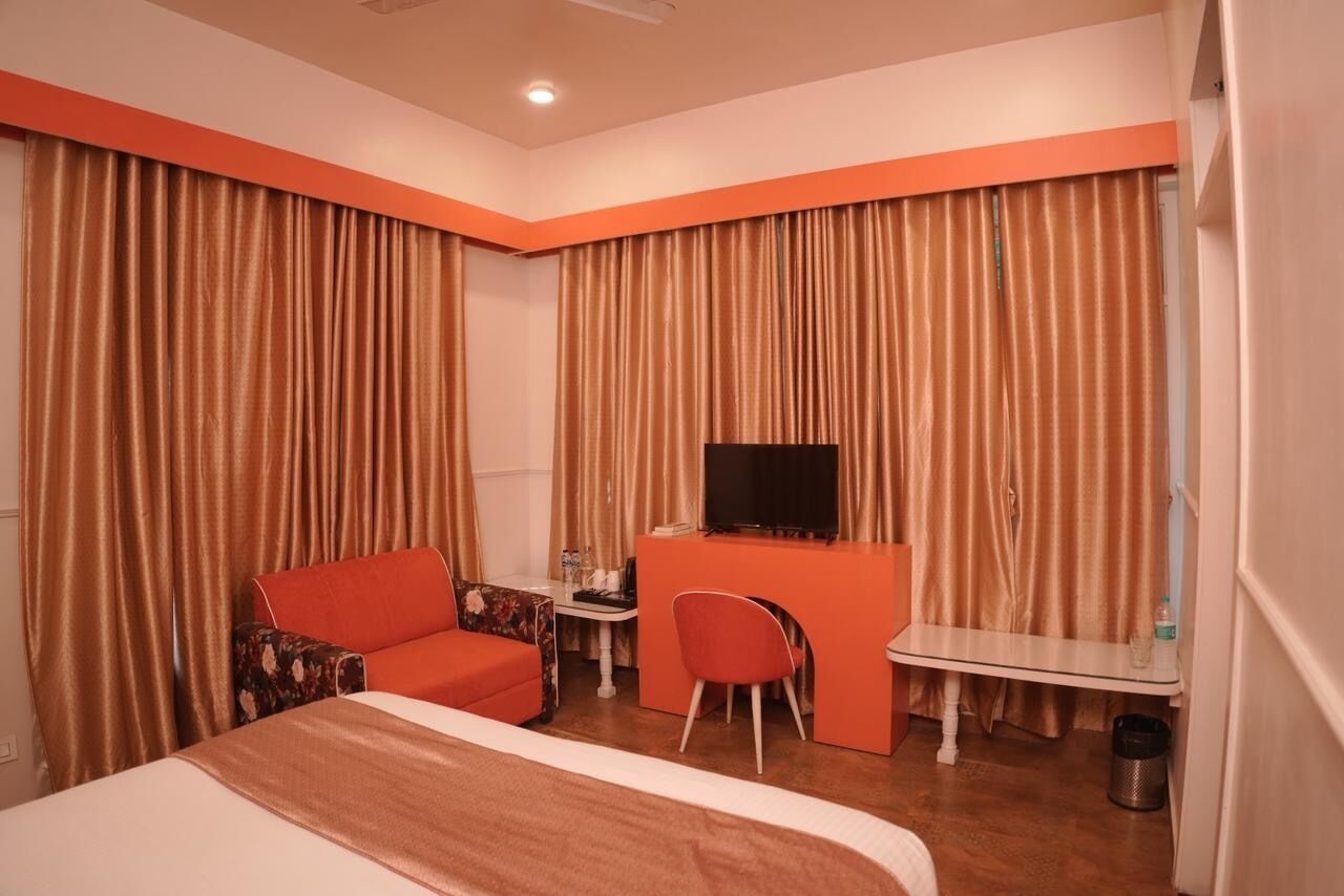 Quarto de hotel com cama, escrivaninha, cadeira, televisão e cortinas.