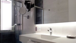 Casa de banho moderna com cabine de duche em vidro, espelho redondo e lavatório branco com saboneteira.