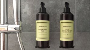 Dois frascos de shampoo e condicionador Woohoo Group para cabelo e corpo sobre uma bancada de banheiro.