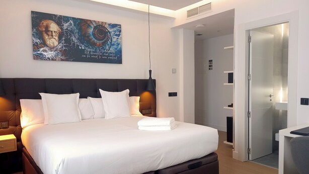 Cama bem arrumada com lençóis brancos, cabeceira escura e uma obra de arte na parede.