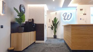 Uma área de recepção com balcão de madeira, máquina de café e um grande letreiro iluminado com a letra 'W'.