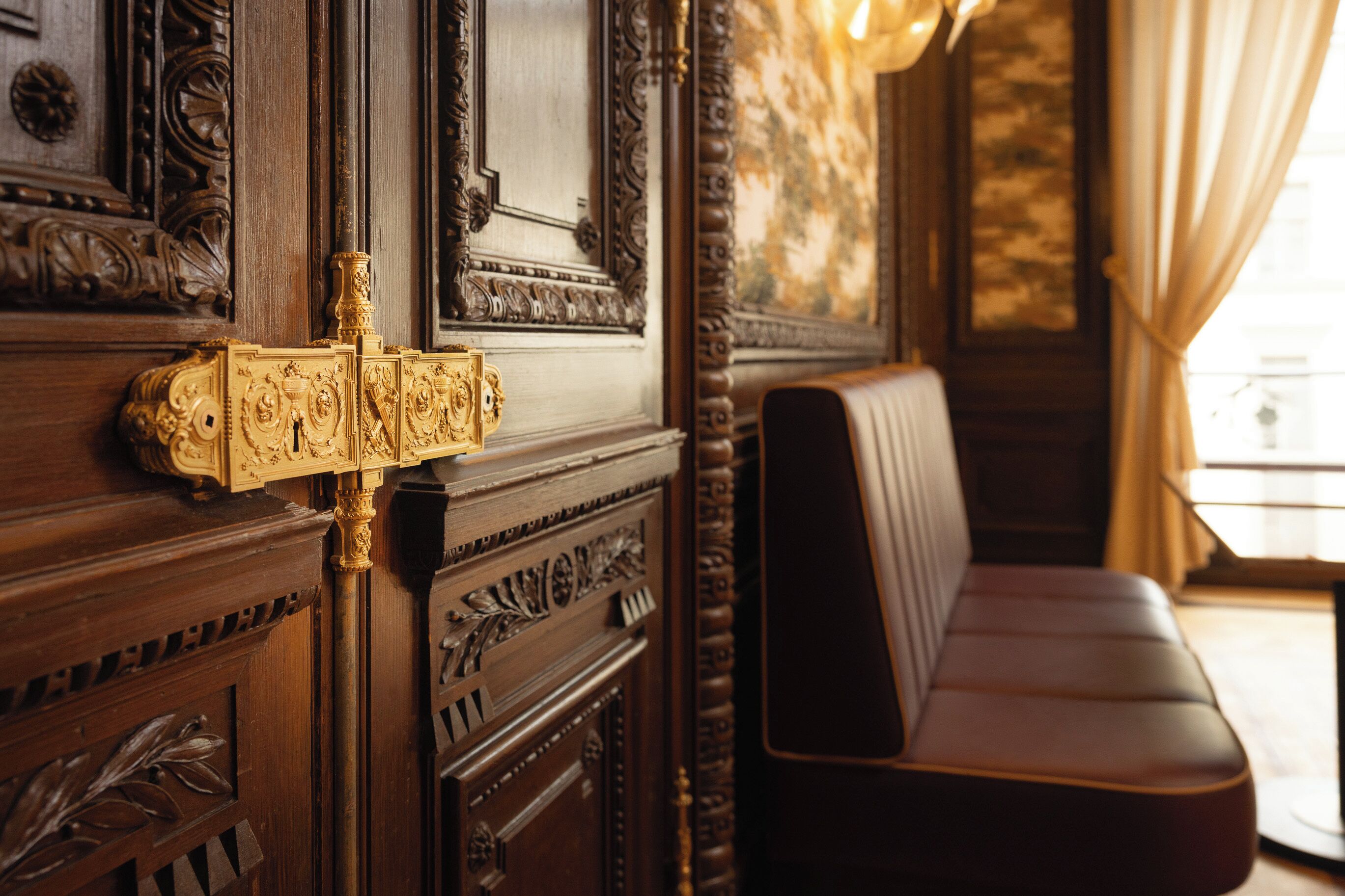 Um banco de madeira com entalhes detalhados, uma porta dourada com desenhos ornamentados e uma parede com textura.