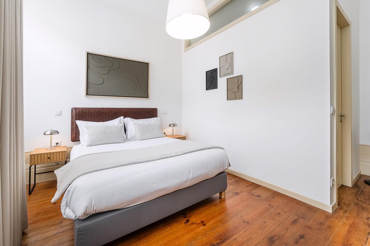 Um quarto com cama, mesas de cabeceira, abajur e obras de arte na parede.