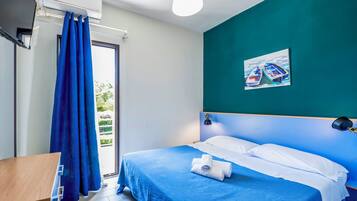 Quarto de hotel com cama, escrivaninha, janela com cortinas, um quadro na parede e uma luminária no teto.