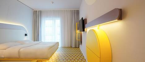Quarto de hotel moderno com uma cama grande, televisão de tela plana na parede e piso estampado.