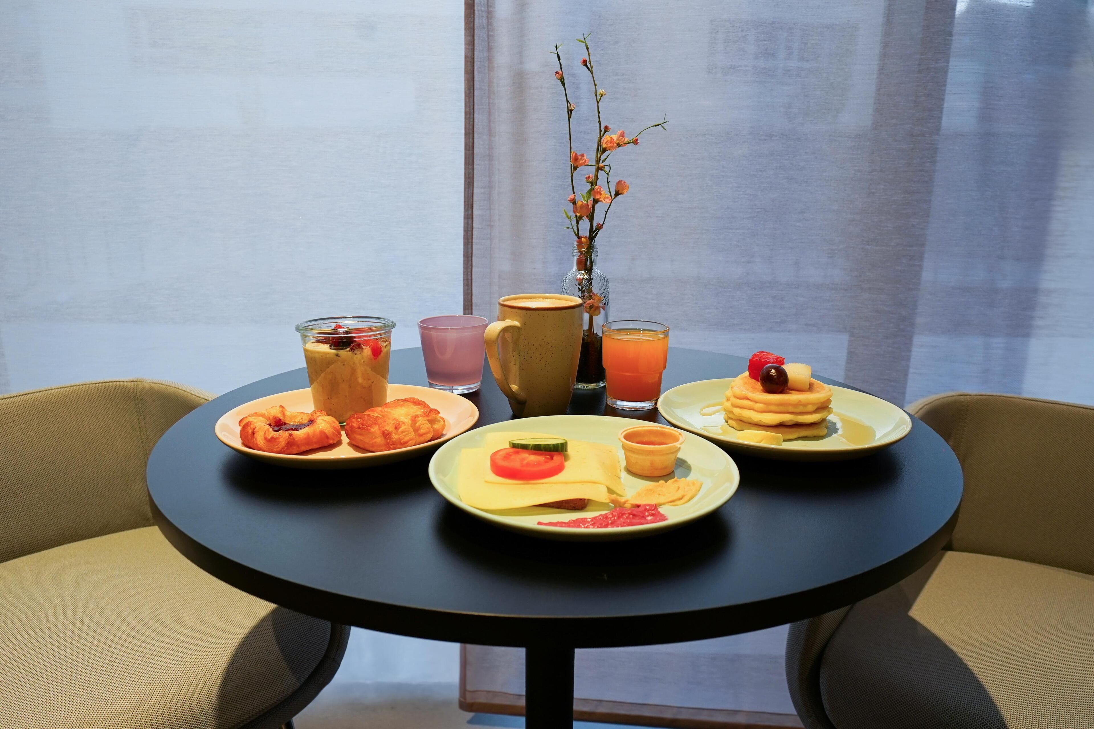 Uma mesa redonda com pratos de comida, um vaso com flores e vista pela janela.