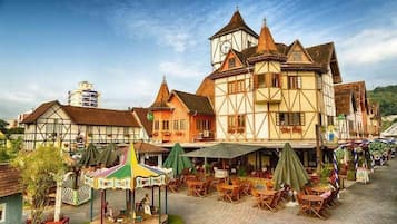 Uma praça tradicional de cidade europeia com um edifício saliente de estrutura de madeira e áreas de estar ao ar livre, e um carrossel colorido.
