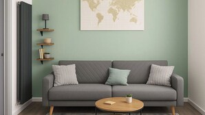 Uma sala de estar com um sofá cinzento, uma mesa de centro redonda de madeira, um mapa-múndi na parede e um radiador.