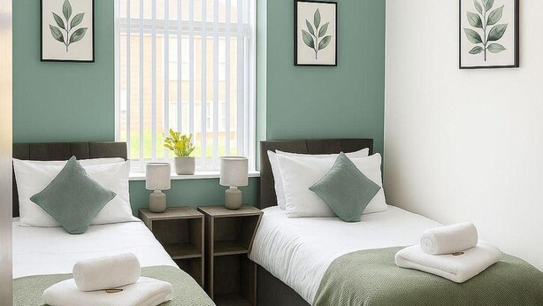 Quarto duplo com duas camas, mesas de cabeceira, luminárias e quadros com folhagens nas paredes.