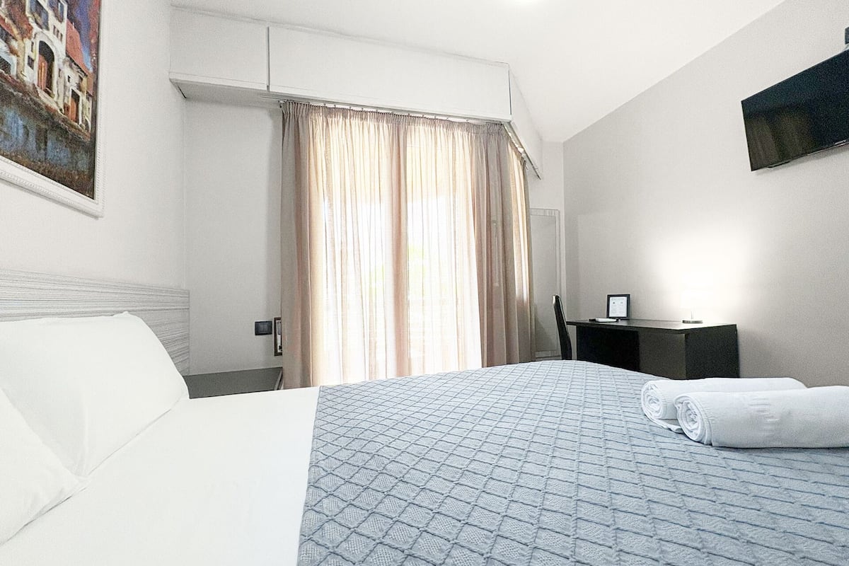 Quarto de hotel com uma cama grande, uma escrivaninha, uma cadeira, televisão de tela plana e um quadro na parede.