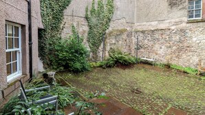 Pátio com muro de pedra, um banco e diversas plantas.