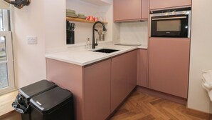 Uma cozinha compacta com armários cor-de-rosa, forno de aço inoxidável e bancada branca.