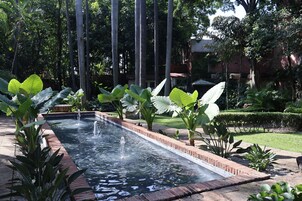 Uma fonte retangular com duas fontes, cercada por um rodapé de tijolos e diversas plantas tropicais.