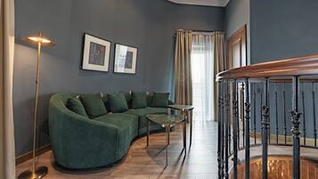 Uma sala de estar moderna com um sofá verde curvo, um abajur, uma mesinha e uma escada com grades ornamentadas.