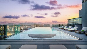 Piscina no terraço com espreguiçadeiras, guarda-corpo de vidro e vista para a cidade.