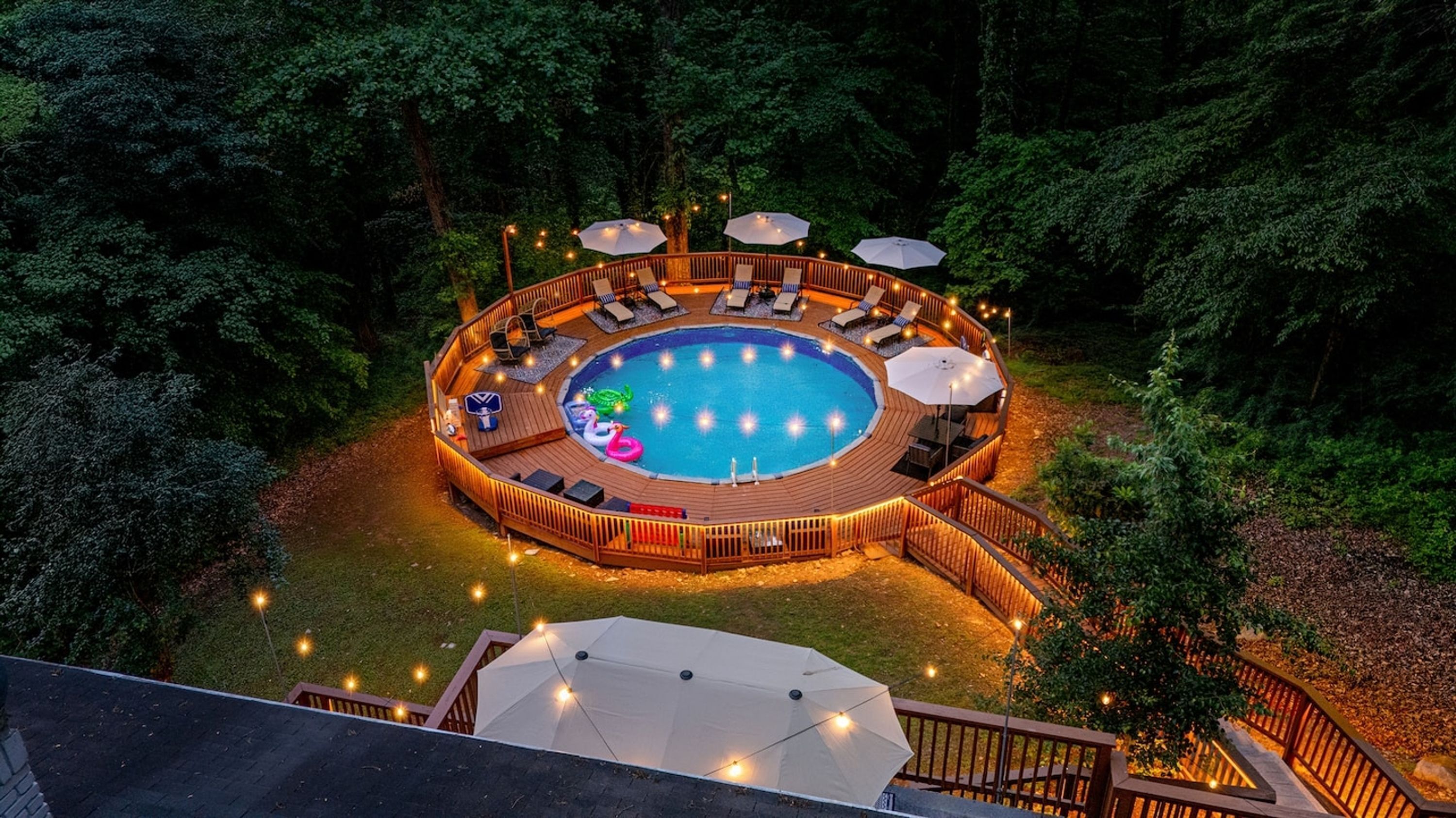Uma piscina circular ao ar livre com deck de madeira, rodeada por espreguiçadeiras e guarda-sóis.