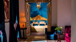 Quarto com cama, lustre, parede azul e vista para o exterior.