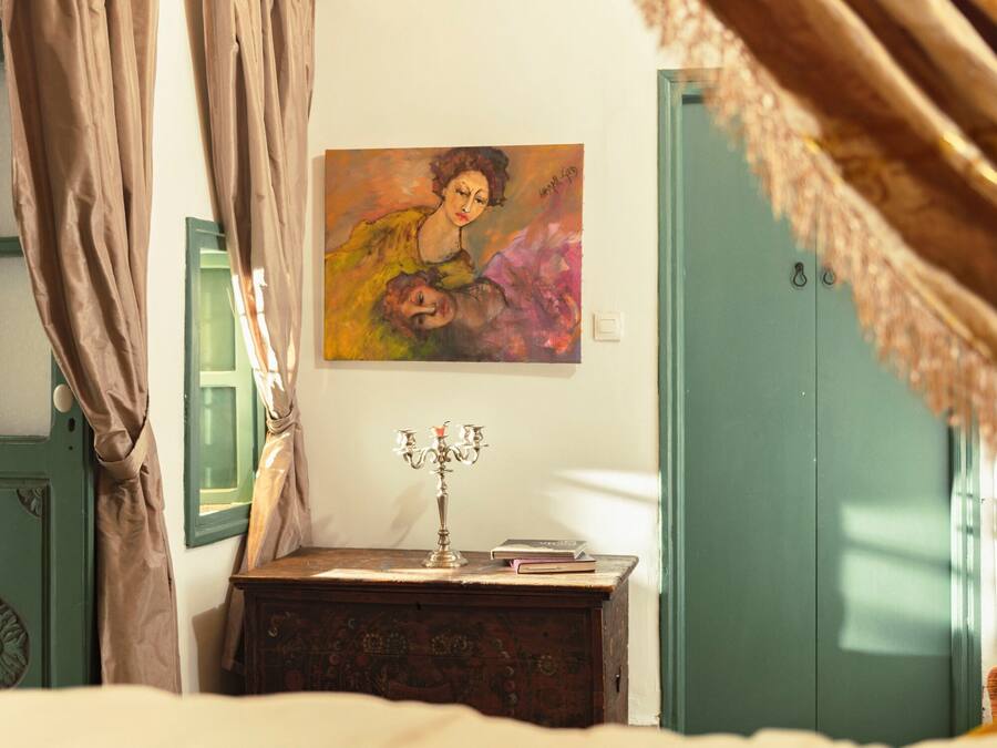 Um quarto com uma cama, uma mesa de cabeceira com castiçal, um quadro e um guarda-roupa verde.