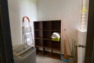 Uma área de lavanderia com máquina de lavar, varal, vassoura e prateleira com produtos de limpeza.