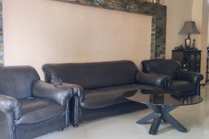 Sala de estar com sofá de couro preto, mesa de centro de vidro e abajur sobre um aparador.