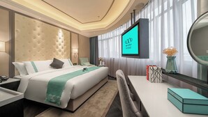 Quarto de hotel moderno com uma cama grande, uma escrivaninha, uma cadeira, uma televisão e uma janela ampla com cortinas.